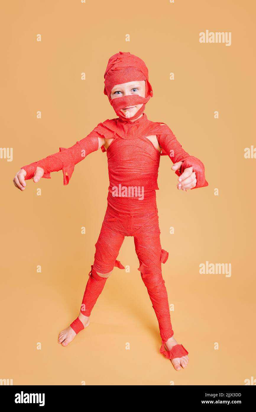 Full body of little boy in red mummy costume making face and raising ...