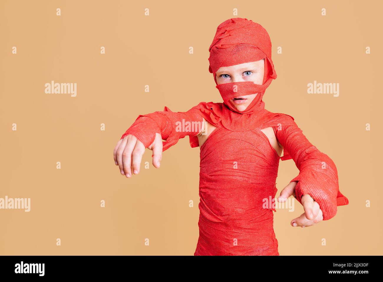 Little boy in red mummy costume making face and raising arms while ...