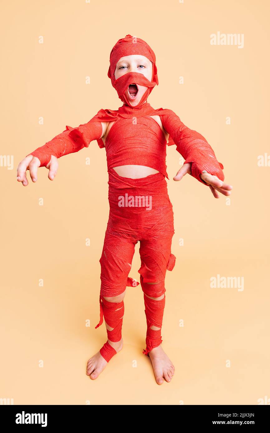 Full body of little boy in red mummy costume making face and raising ...