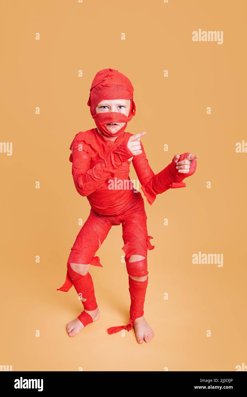 Full body of little boy in red mummy costume making face and raising ...