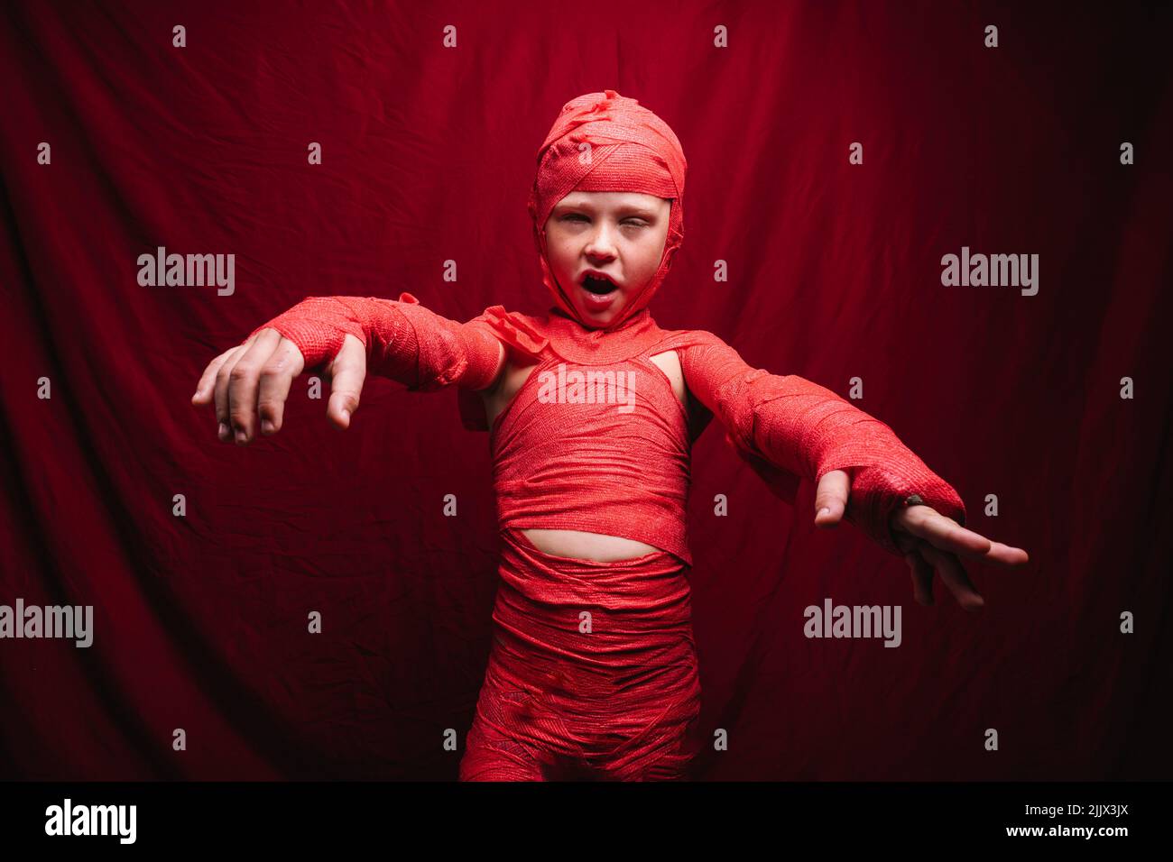 Adorable little boy in red mummy costume making scary face and reaching ...