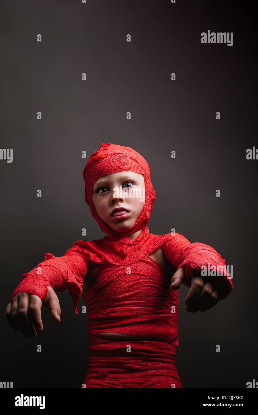 Adorable little boy in red mummy costume making scary face and reaching ...