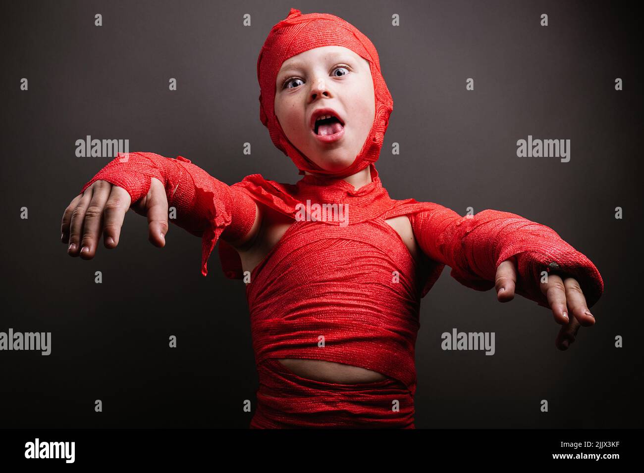 Adorable little boy in red mummy costume making scary face and reaching ...
