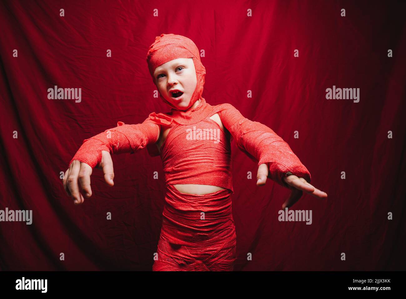 Adorable little boy in red mummy costume making scary face and reaching ...