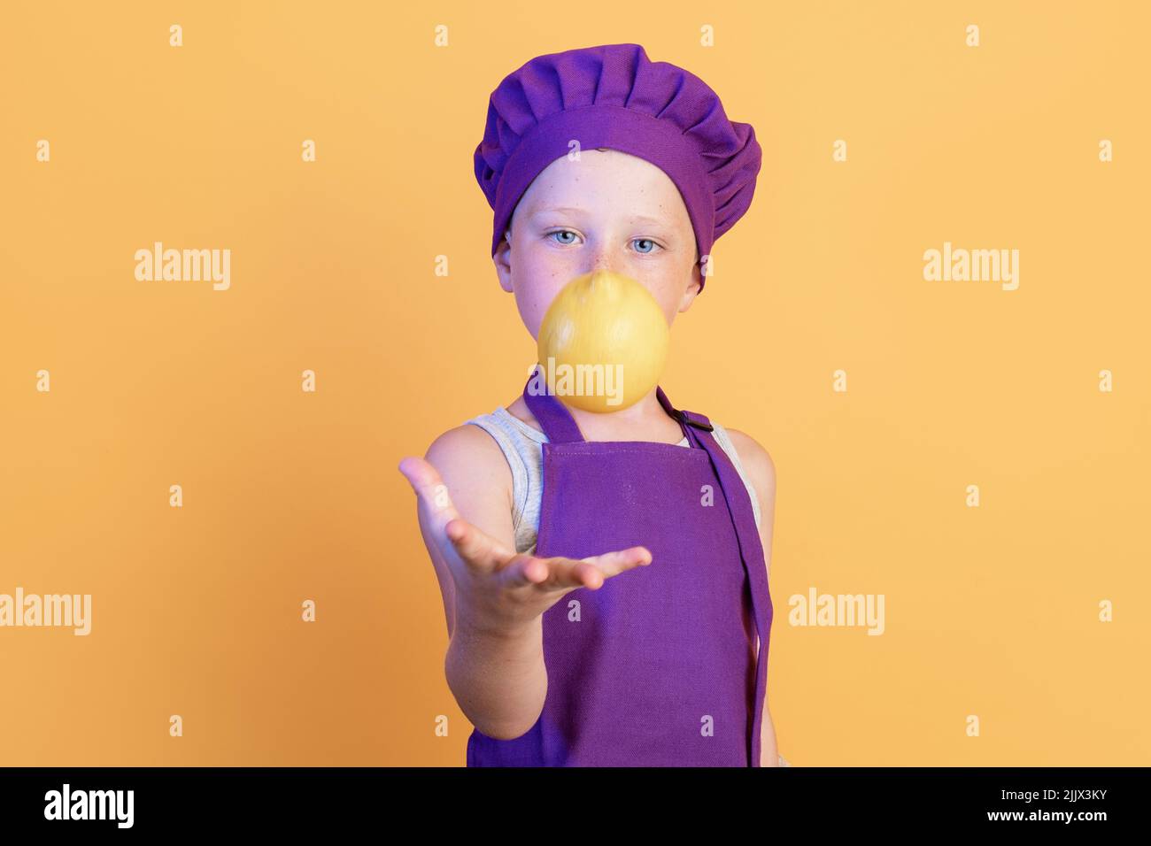 Little child in purple chef apron and hat looking at camera throwing ...