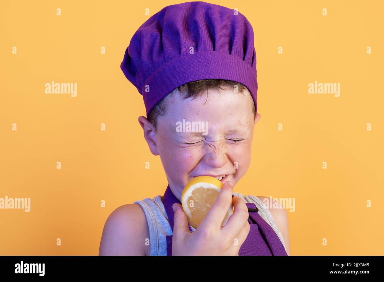Finny little boy in purple chef hat and apron screwing up eyes while ...