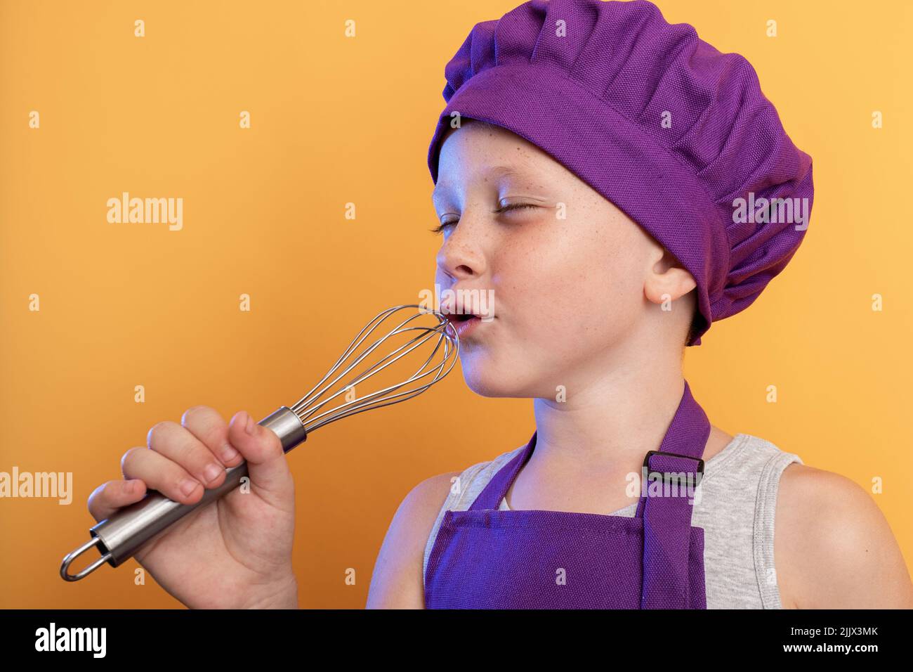 Cheerful boy in purple chef uniform singing into metal whisk with ...