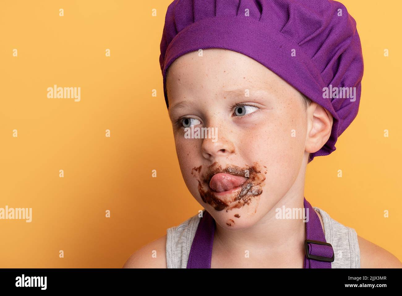 Messy boy in purple chef uniform with sweet chocolate on mouth looking ...