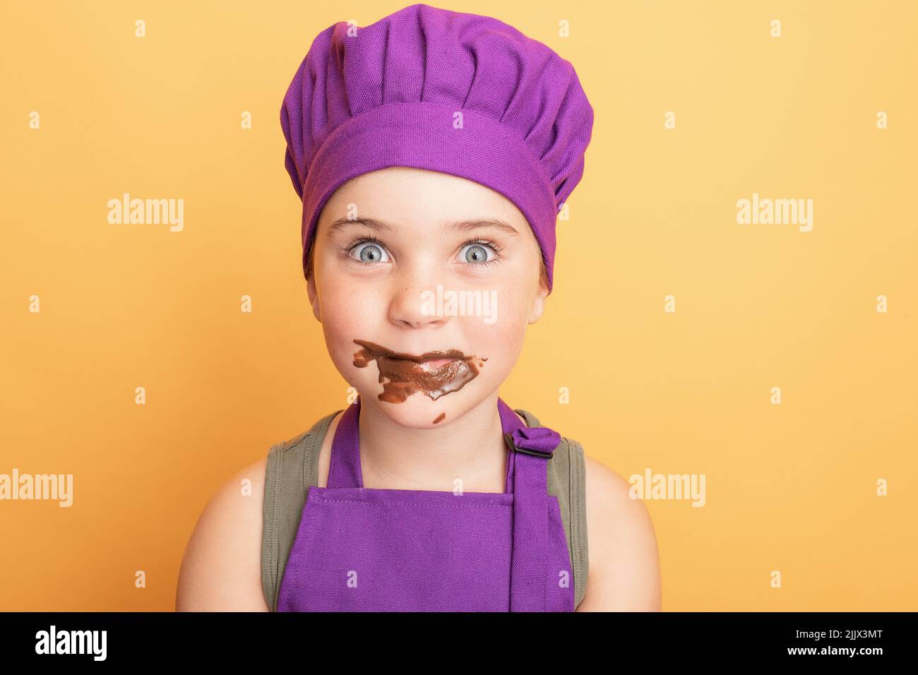 Astonished messy girl in purple chef uniform with sweet chocolate on ...