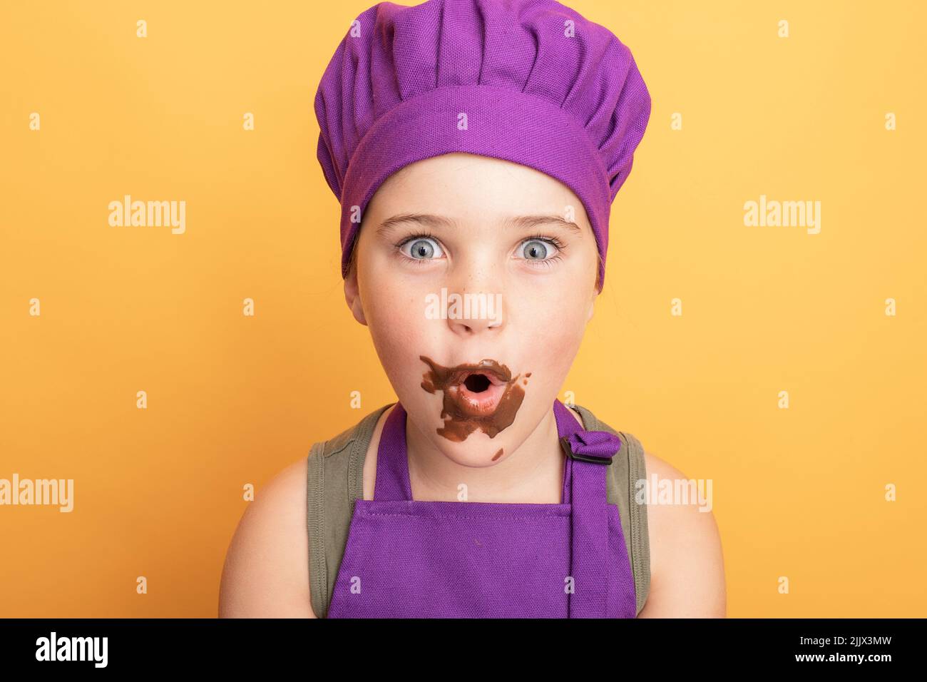 Astonished messy girl in purple chef uniform with sweet chocolate on ...