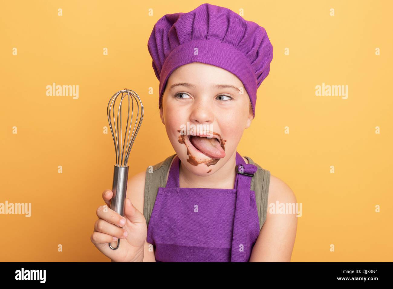 Cute smiling dirty boy in chef uniform looking at camera holding whisk ...