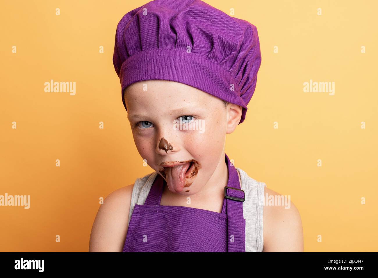 Astonished messy boy in purple chef uniform with sweet chocolate on ...