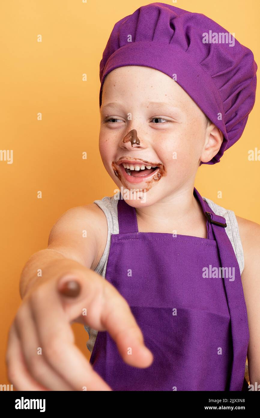 Laughing boy in purple chef uniform with face covered with chocolate ...