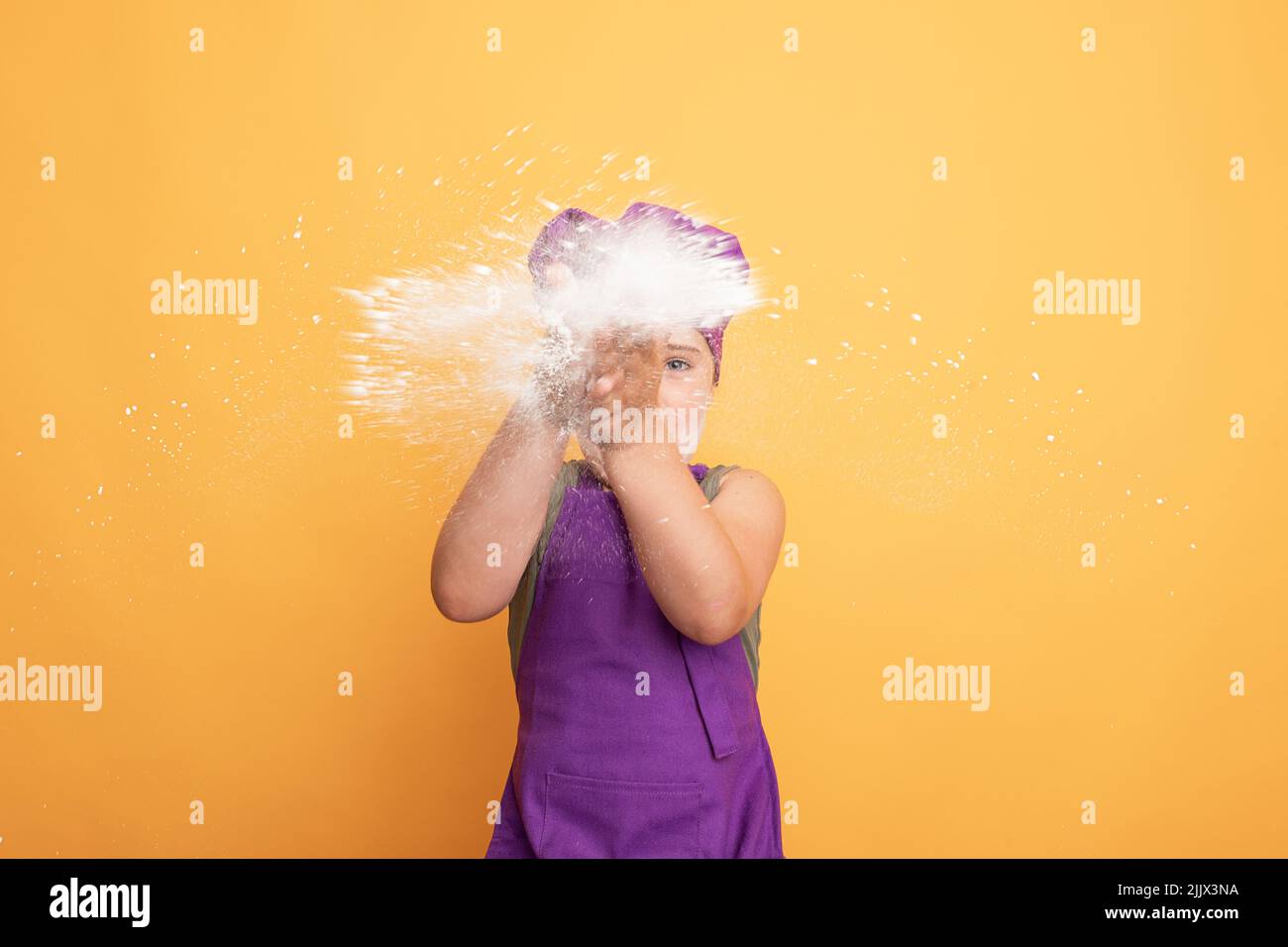Optimistic girl in purple chef uniform clapping hands with white flour ...