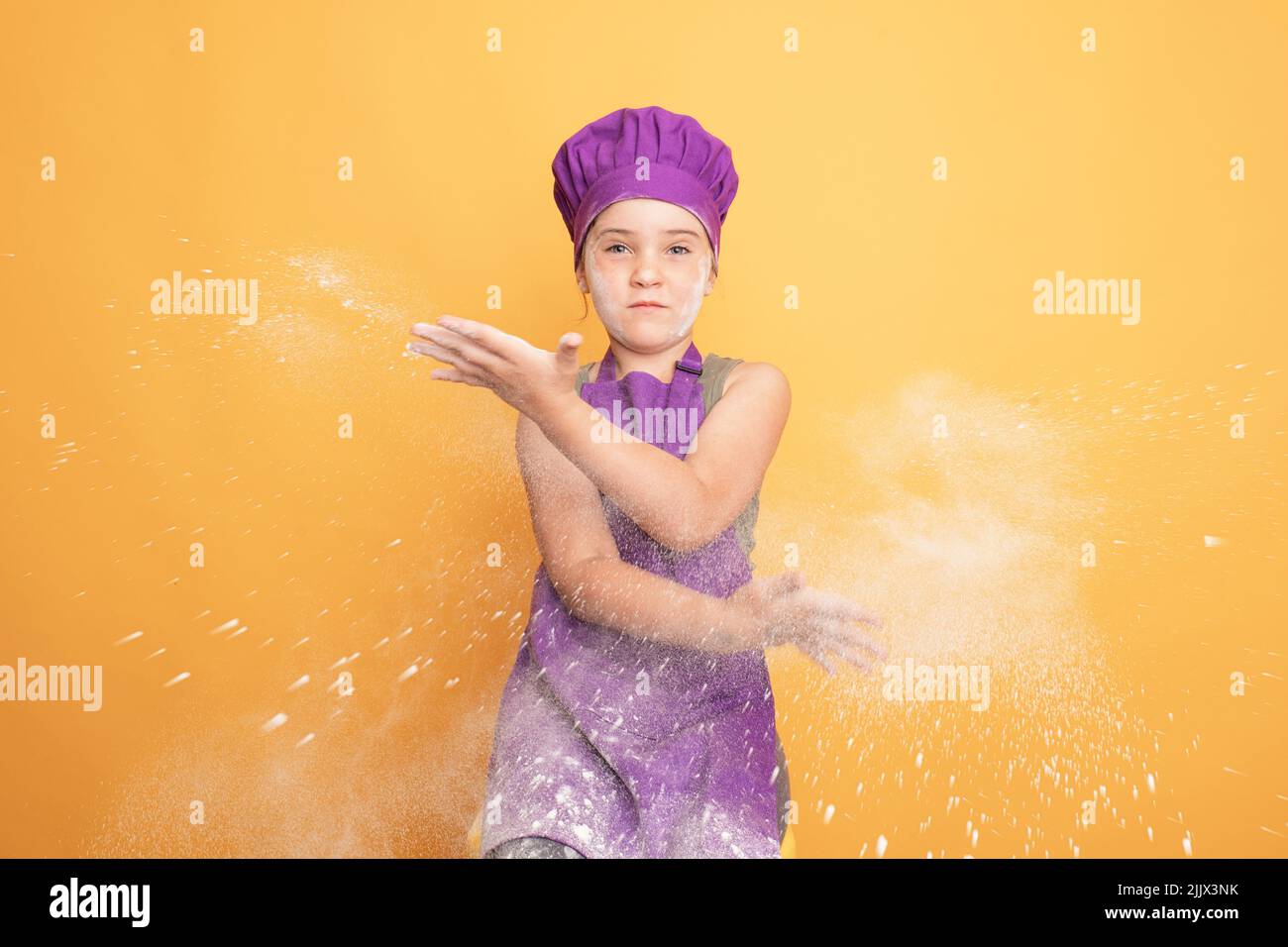 Optimistic girl in purple chef uniform clapping hands with white flour ...