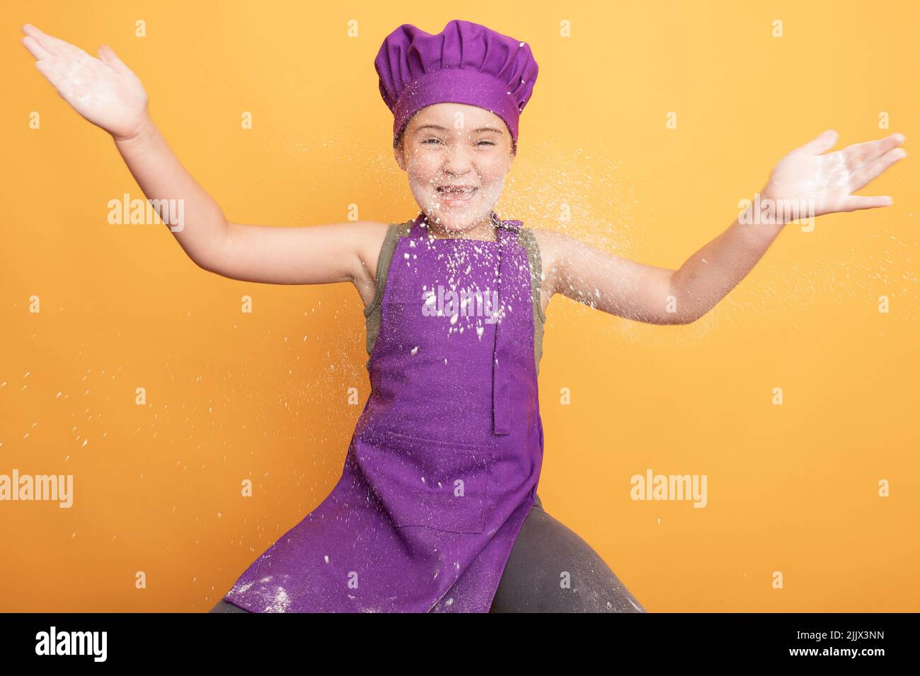 Optimistic girl in purple chef uniform clapping hands with white flour ...