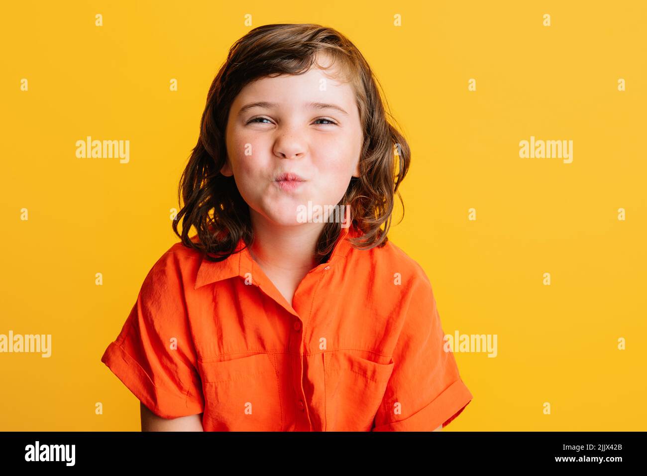 Adorable little girl in orange shirt looking at camera and pouting lips ...