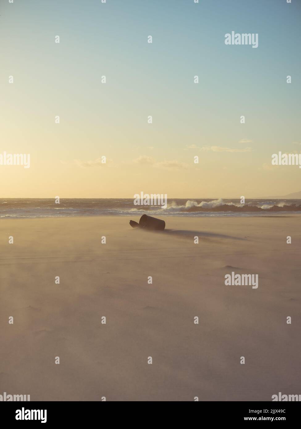 Ground level of tin dumped on dry sand against waving sea and sunset ...