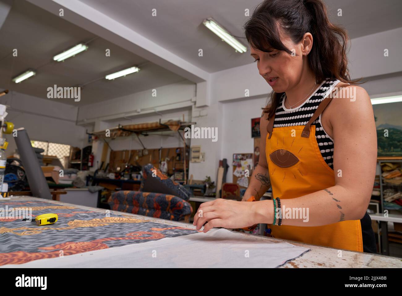 Positive adult tattooed female master with dark hair and apron drawing ...