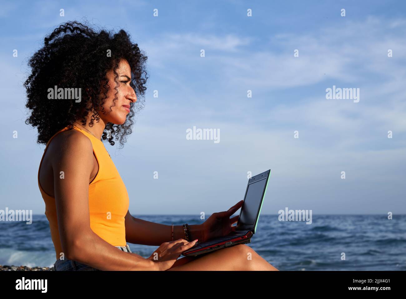Side view of female surfing internet on netbook while sitting on coast ...
