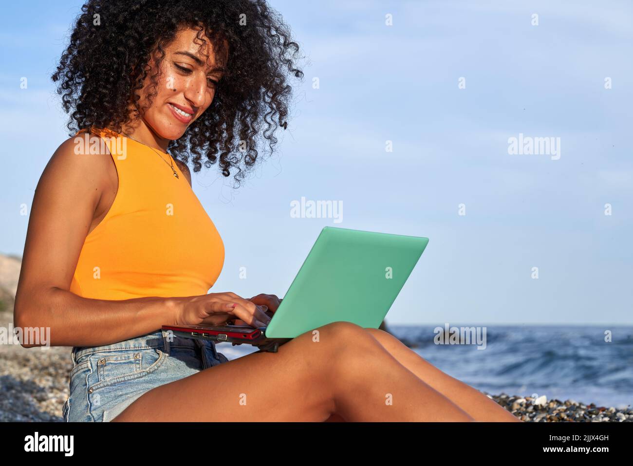Side view of female surfing internet on netbook while sitting on coast ...