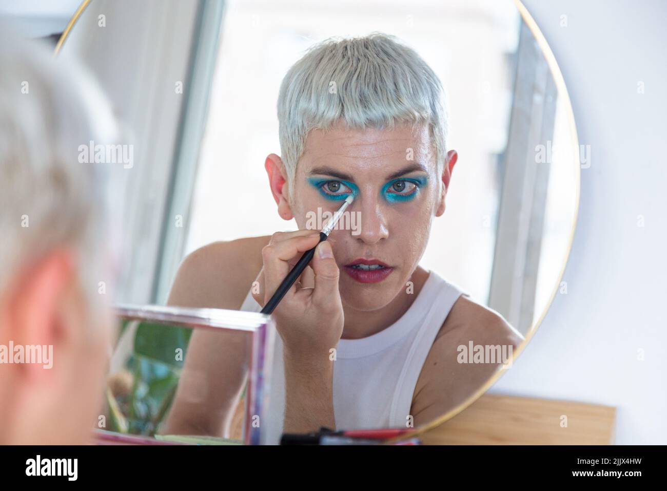 Transgender man wearing blue eyeshadow applying mascara while looking ...