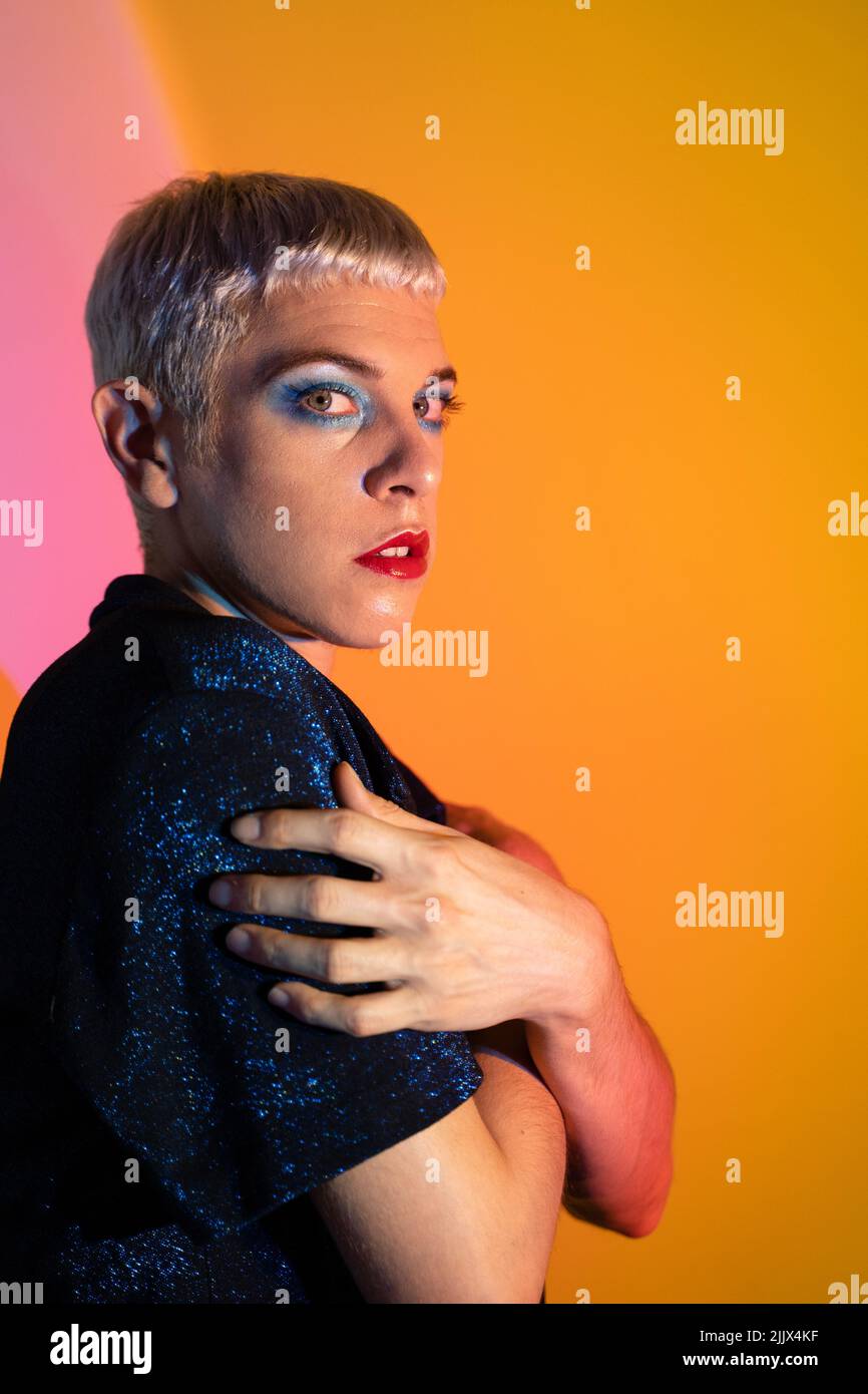 Portrait of transgender man wearing makeup hugging self in illuminated ...