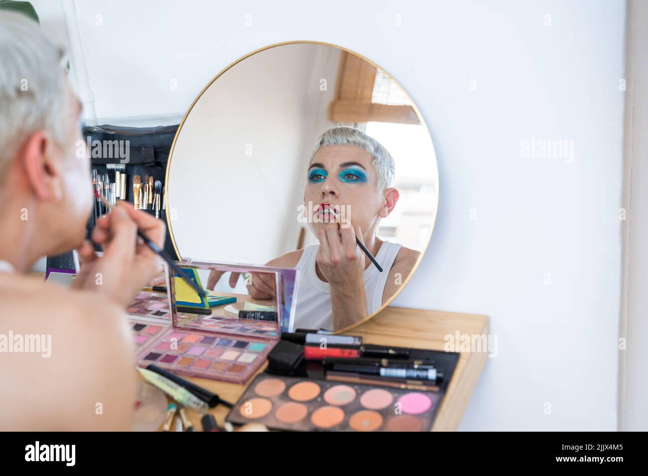 Young transgender looking at mirror and applying lipstick at dressing ...