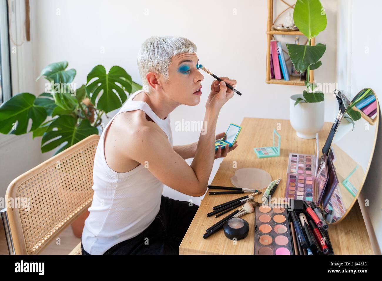 Transgender man wearing blue eyeshadow applying mascara while looking ...
