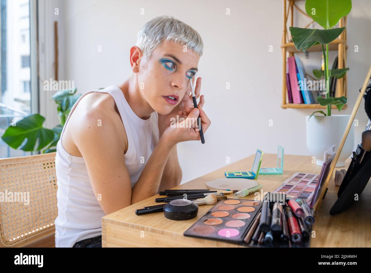 Transgender man wearing blue eyeshadow applying mascara while looking ...