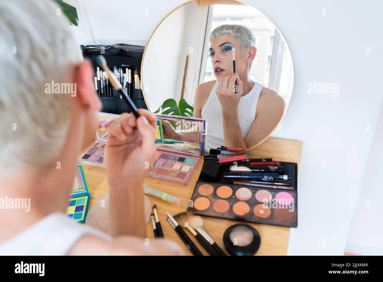 Transgender man wearing blue eyeshadow applying mascara while looking ...