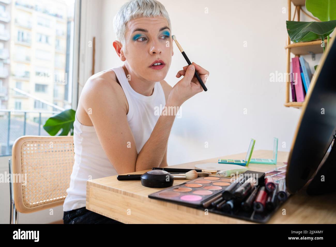 Transgender man wearing blue eyeshadow applying mascara while looking ...