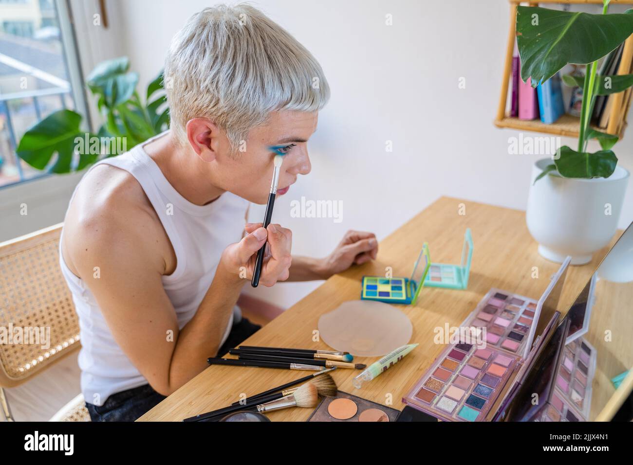 Transgender man wearing blue eyeshadow applying mascara while looking ...