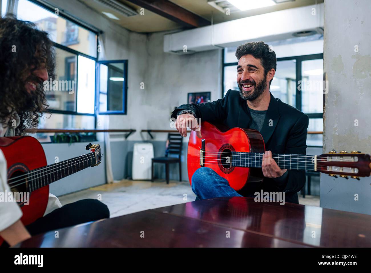 Male friends playing guitars at table in music studio Stock Photo - Alamy