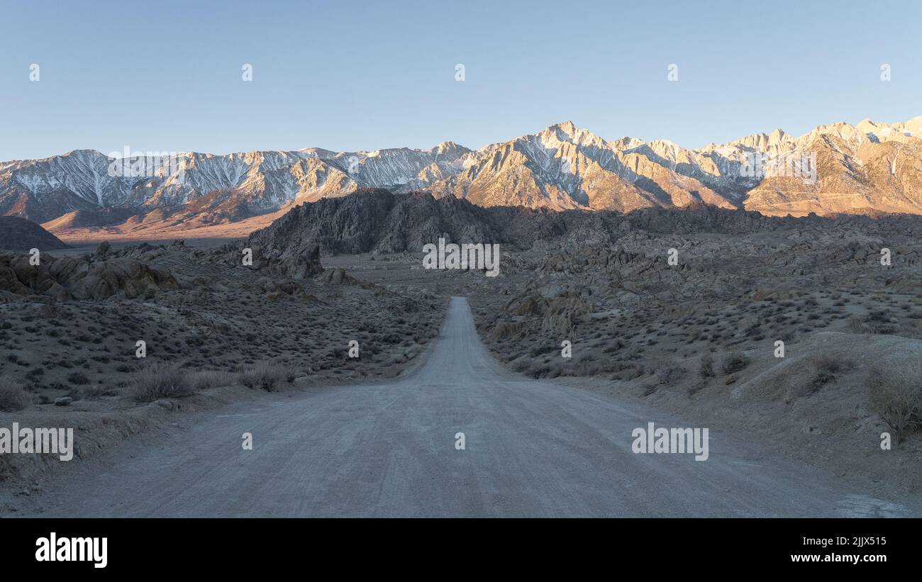 Long empty roadway between dry terrain leading to range of rough rocky ...