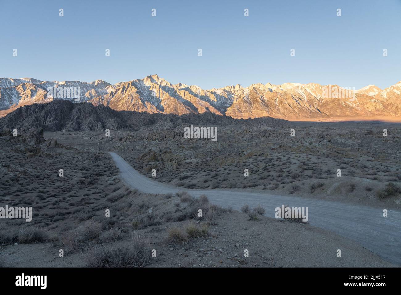 Long empty roadway between dry terrain leading to range of rough rocky ...