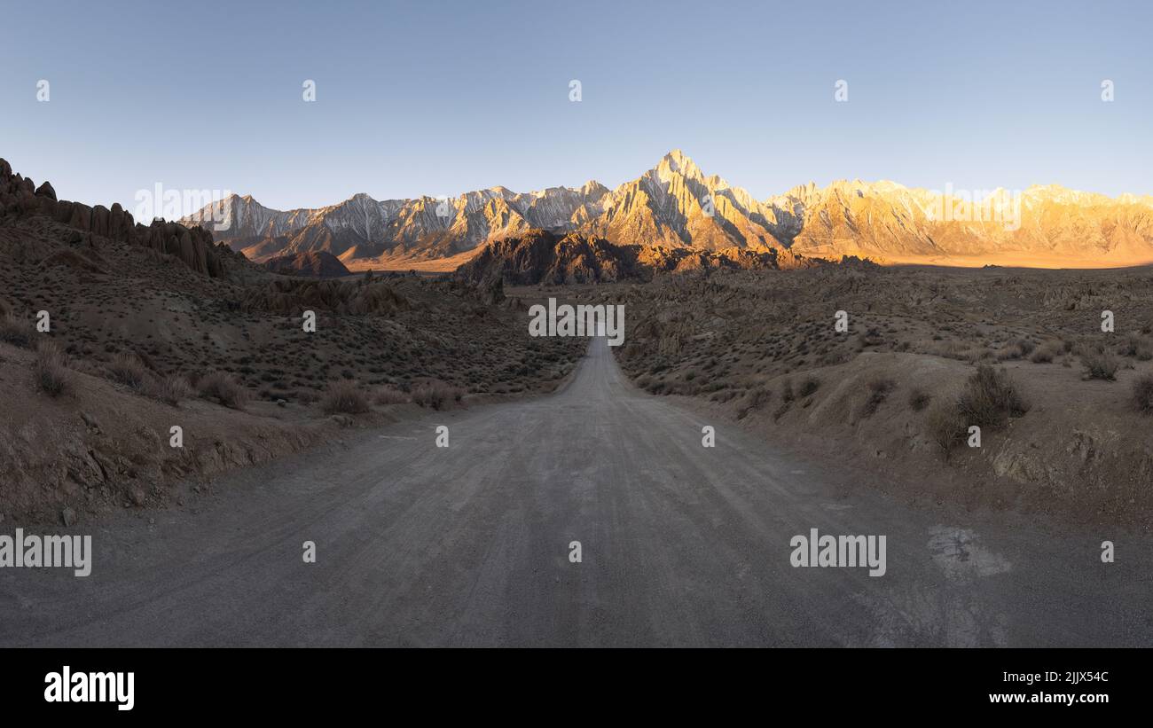 Long empty roadway between dry terrain leading to range of rough rocky ...