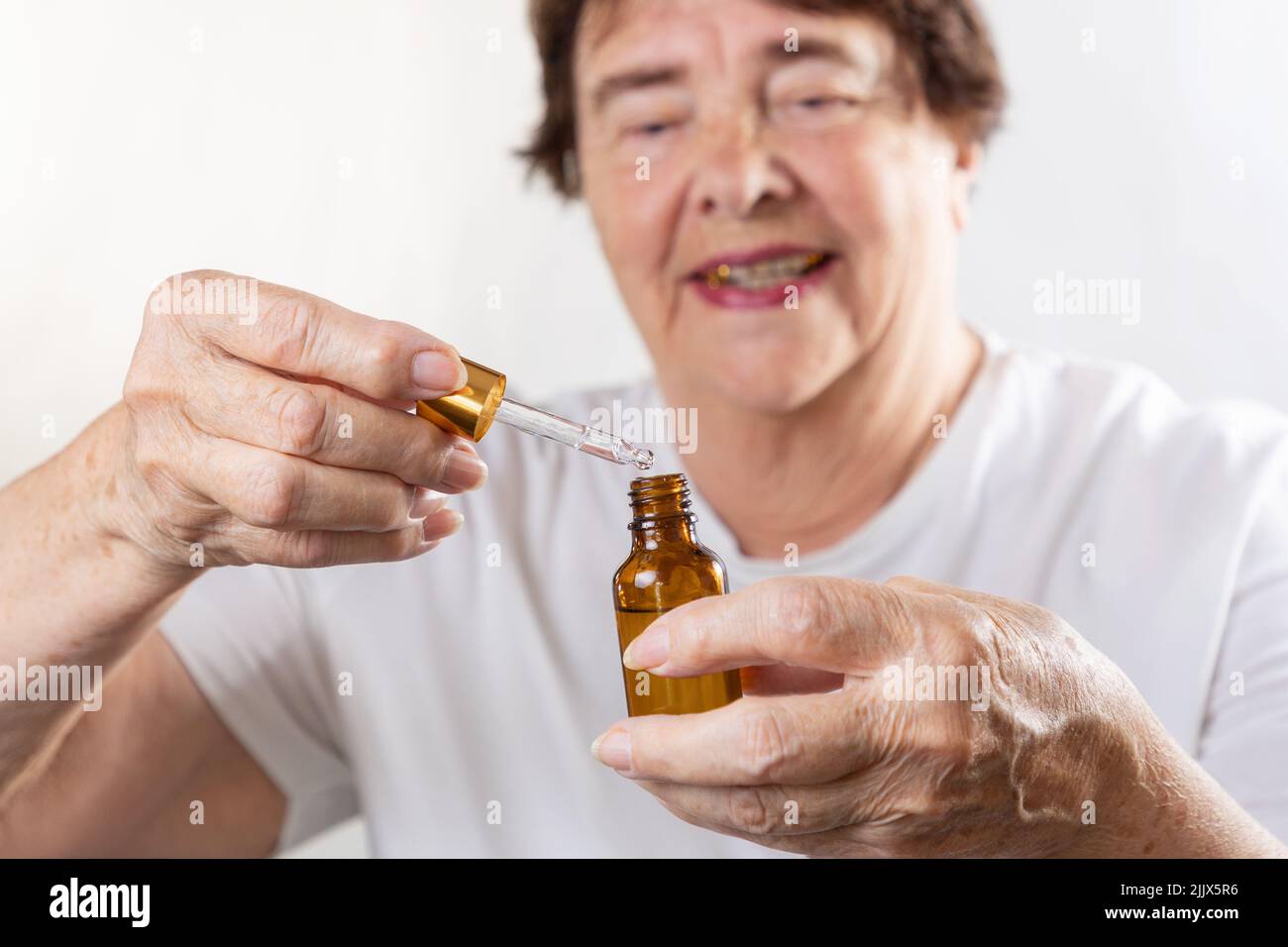 Portrait of an elderly smiling woman holding a facial serum and ...