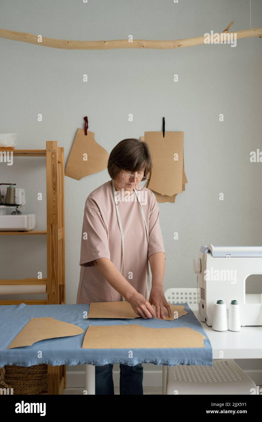 Focused professional dressmaker with measuring tape making patterns on ...