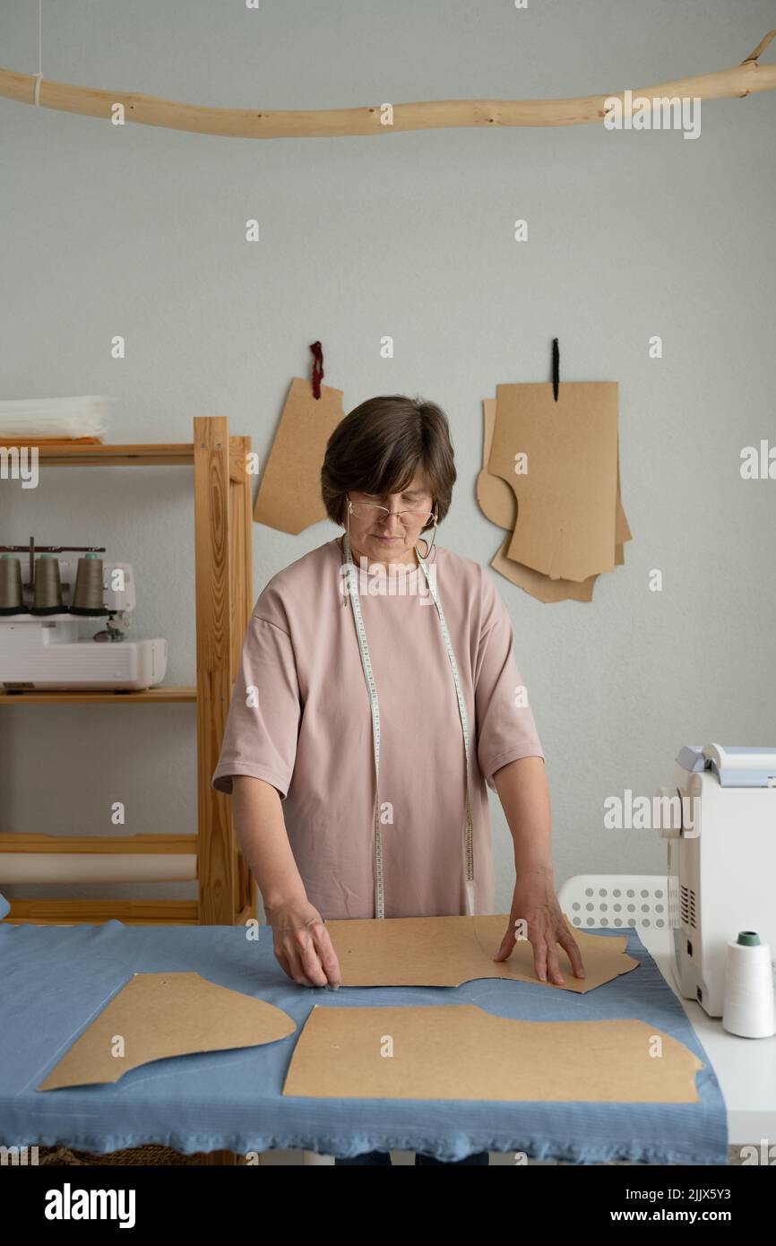 Focused professional dressmaker with measuring tape making patterns on ...