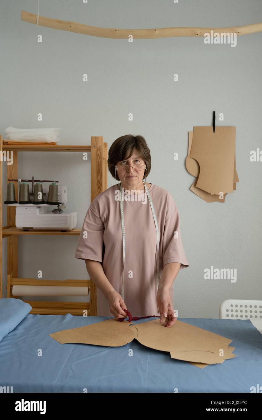 Focused professional dressmaker with measuring tape making patterns on ...