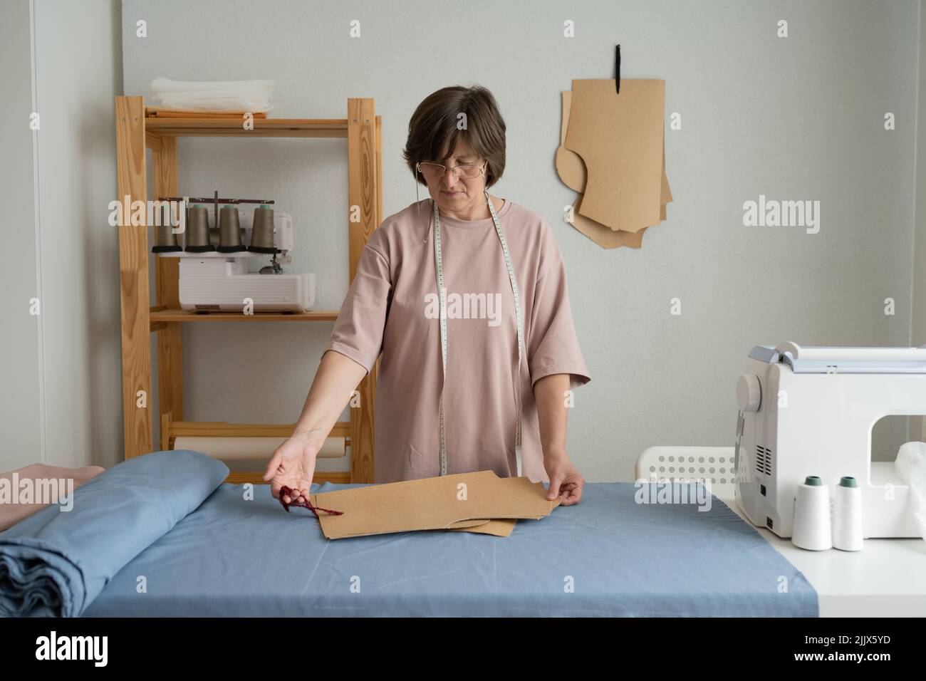 Focused professional dressmaker with measuring tape making patterns on ...