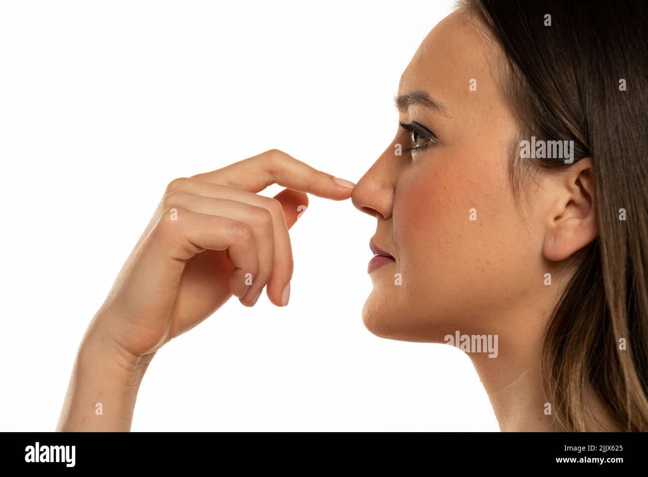 Young woman touches her nose with her finger on a white background ...