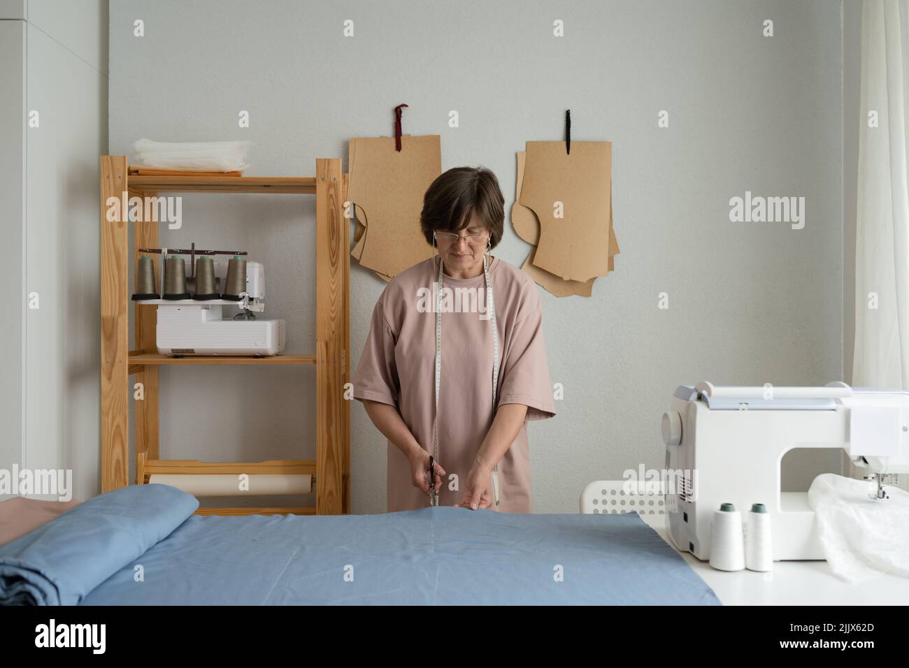 Concentrated professional female dressmaker with measuring tape cutting ...