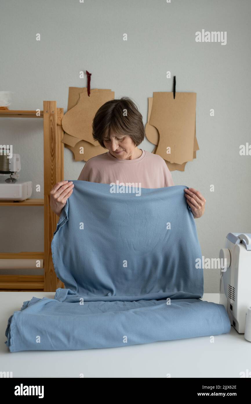 Professional female dressmaker looking at blue textile on table while ...