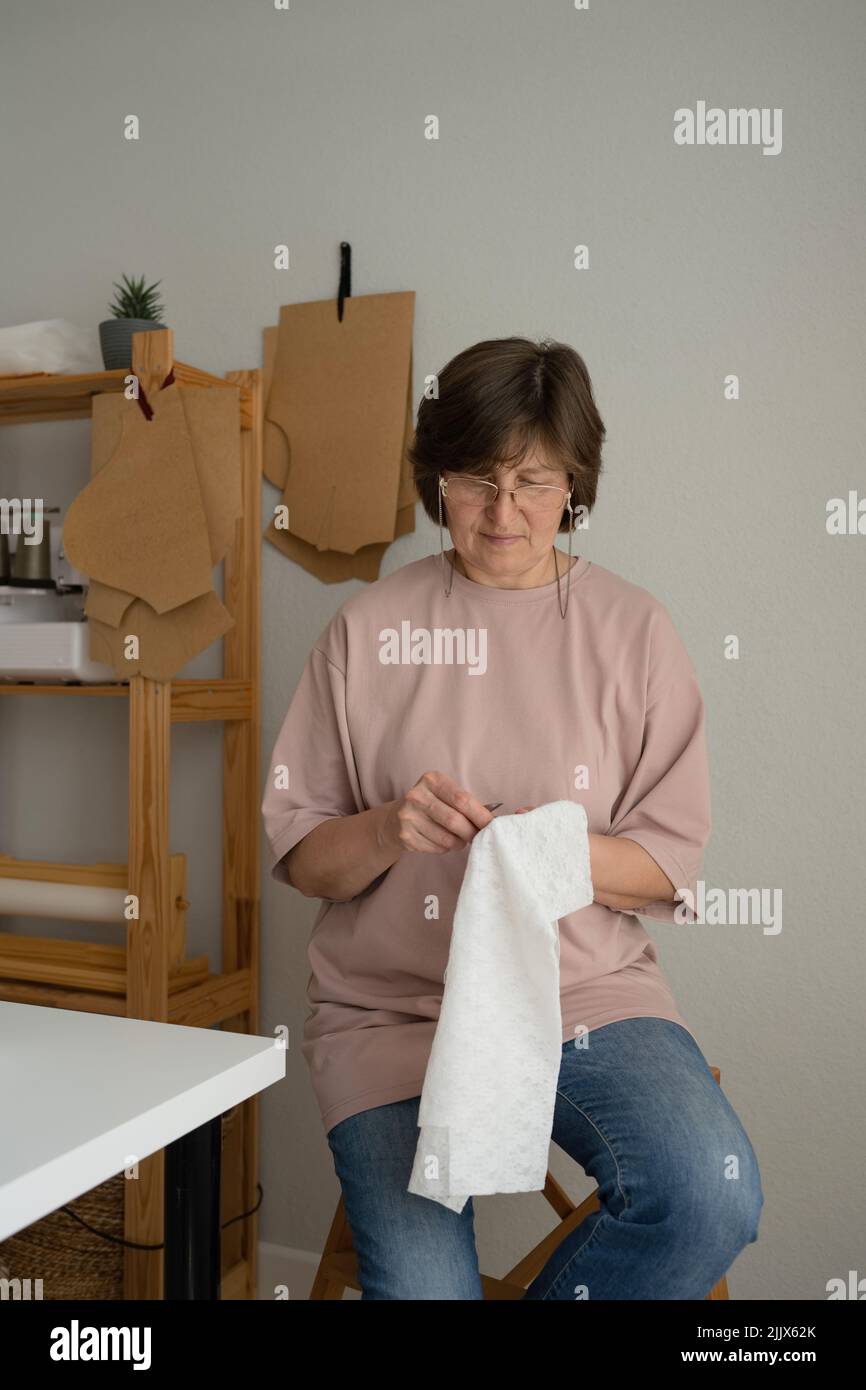 Focused professional female dressmaker in eyeglasses trimming threads ...