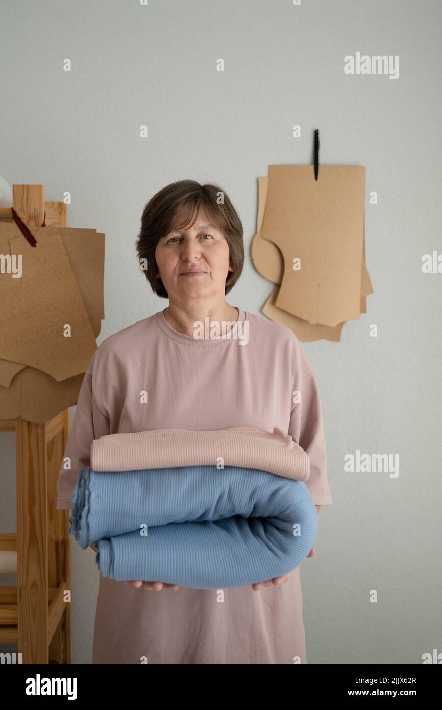 Professional female dressmaker holding bale of textile and looking at ...