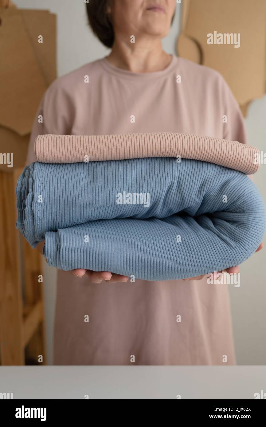 Professional female dressmaker holding bale of textile and looking away ...