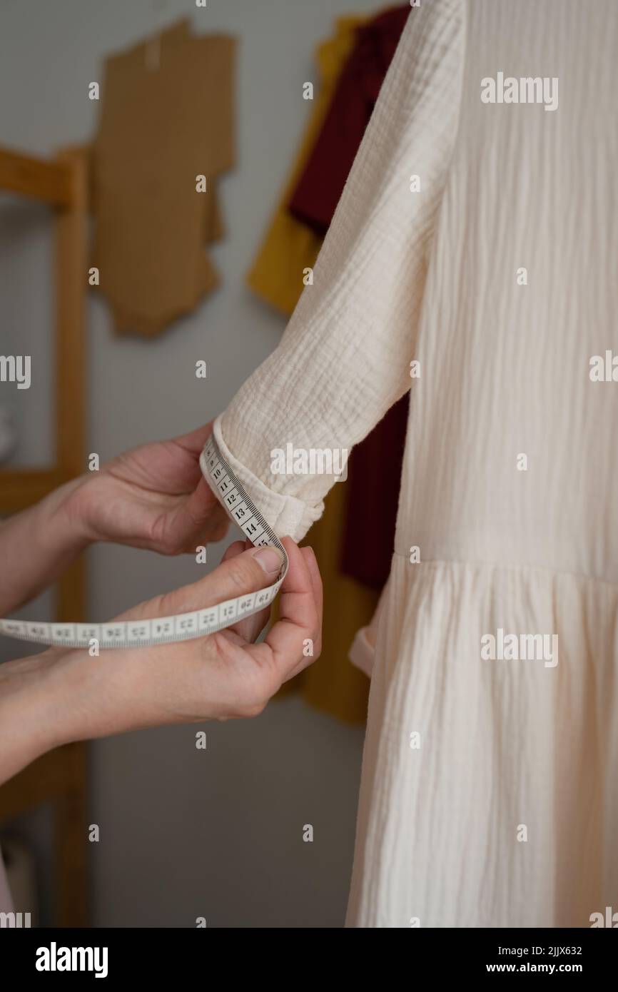 Crop tailor using tape to measure sleeve of handmade white dress while ...