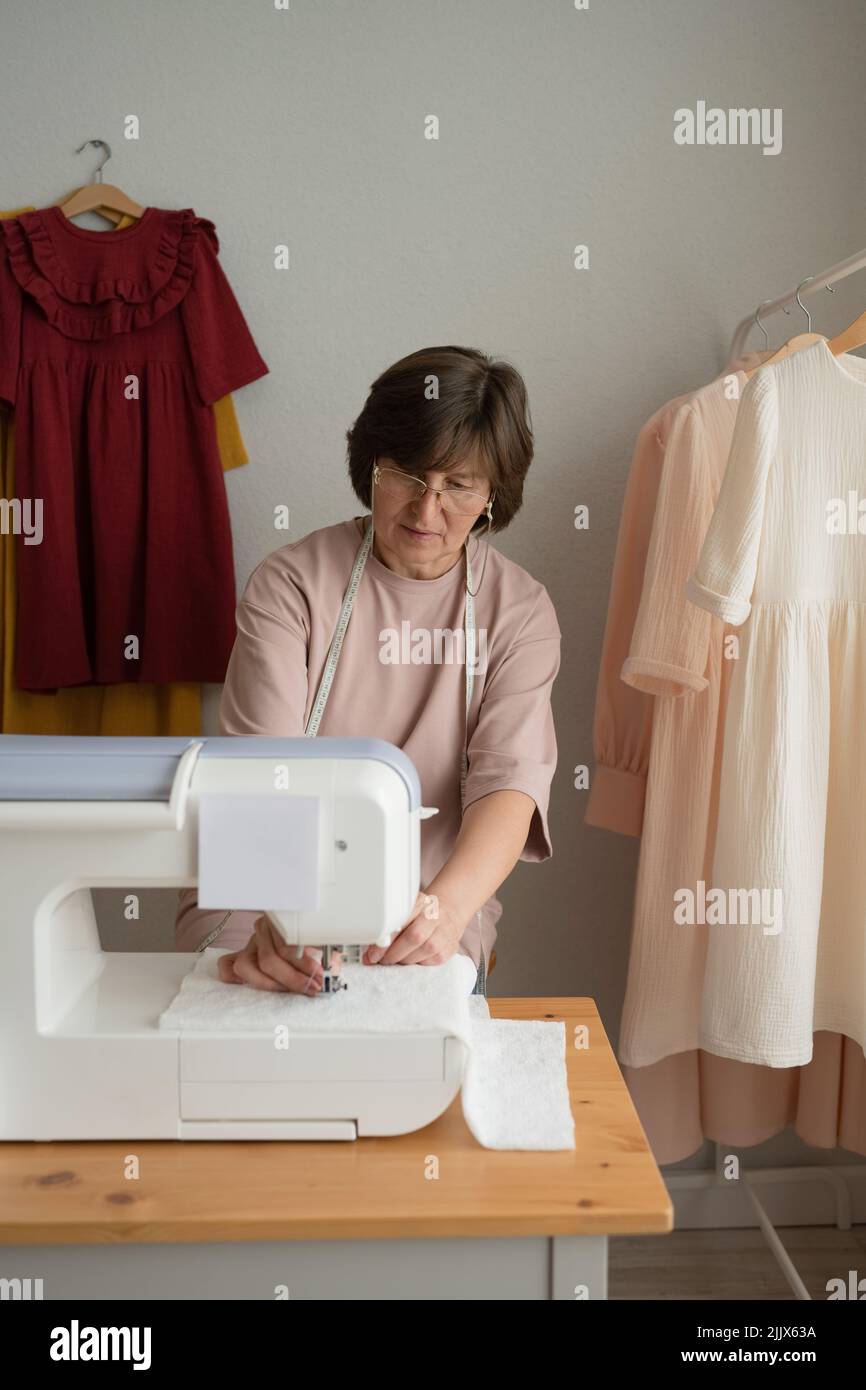 Concentrated female dressmaker in eyeglasses working on sewing machine ...